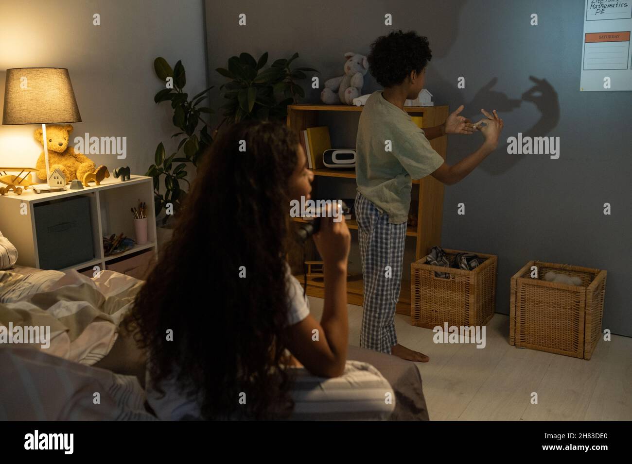 African American boy in pijamas showing hand shadow performance on wall ...