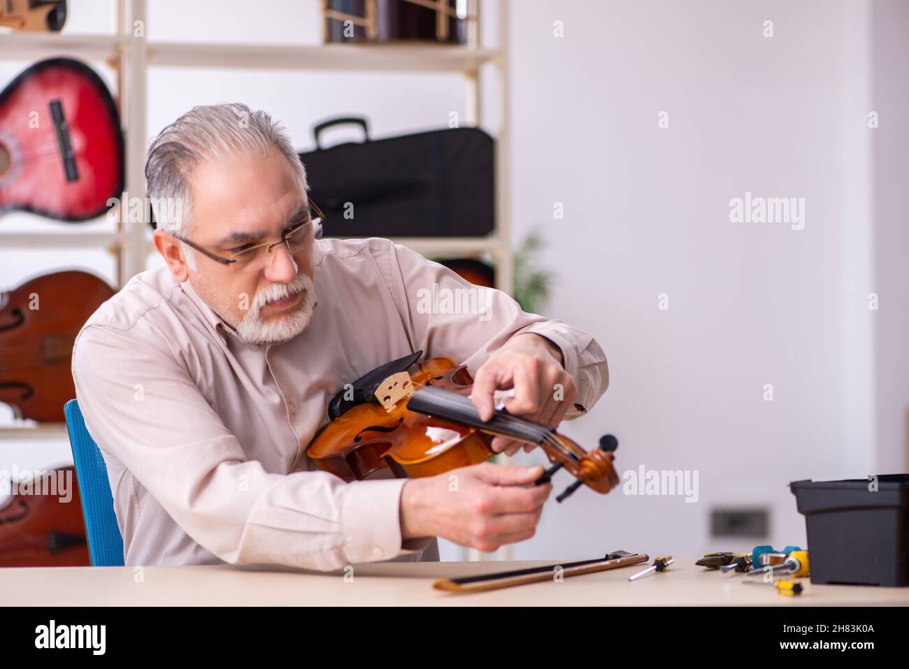 Old repairman repairing musical instruments at workplace Stock Photo ...