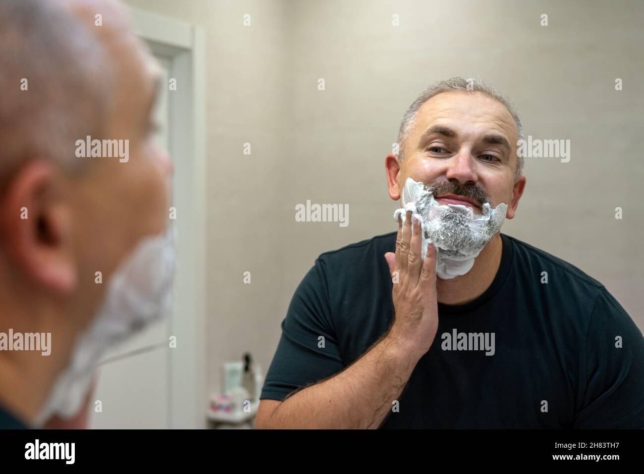Portrait of handsome gray-haired middle-aged man applying shaving foam ...