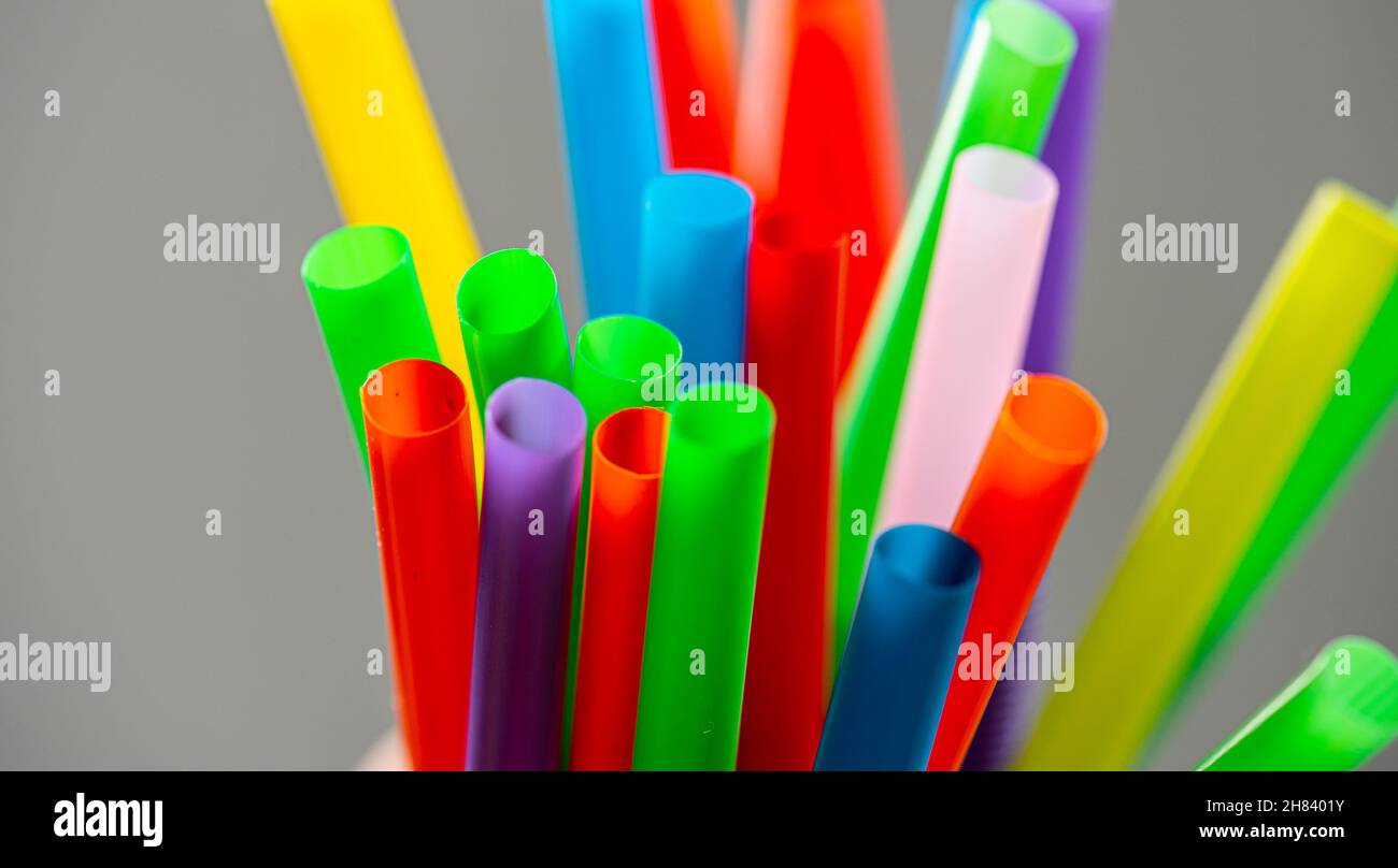 Multi colored plastic straws in a jar in front of a grey background ...