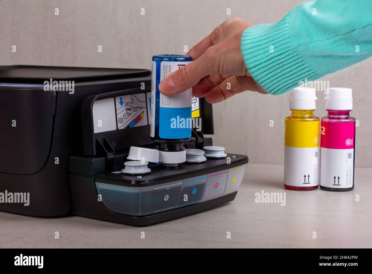 a woman's hand pours blue paint from a bottle into the color printer ...