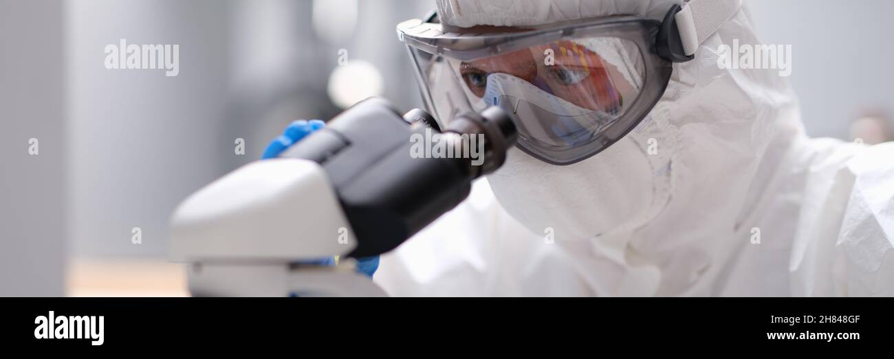 Scientist chemist in protective anti-plague suit looking through ...