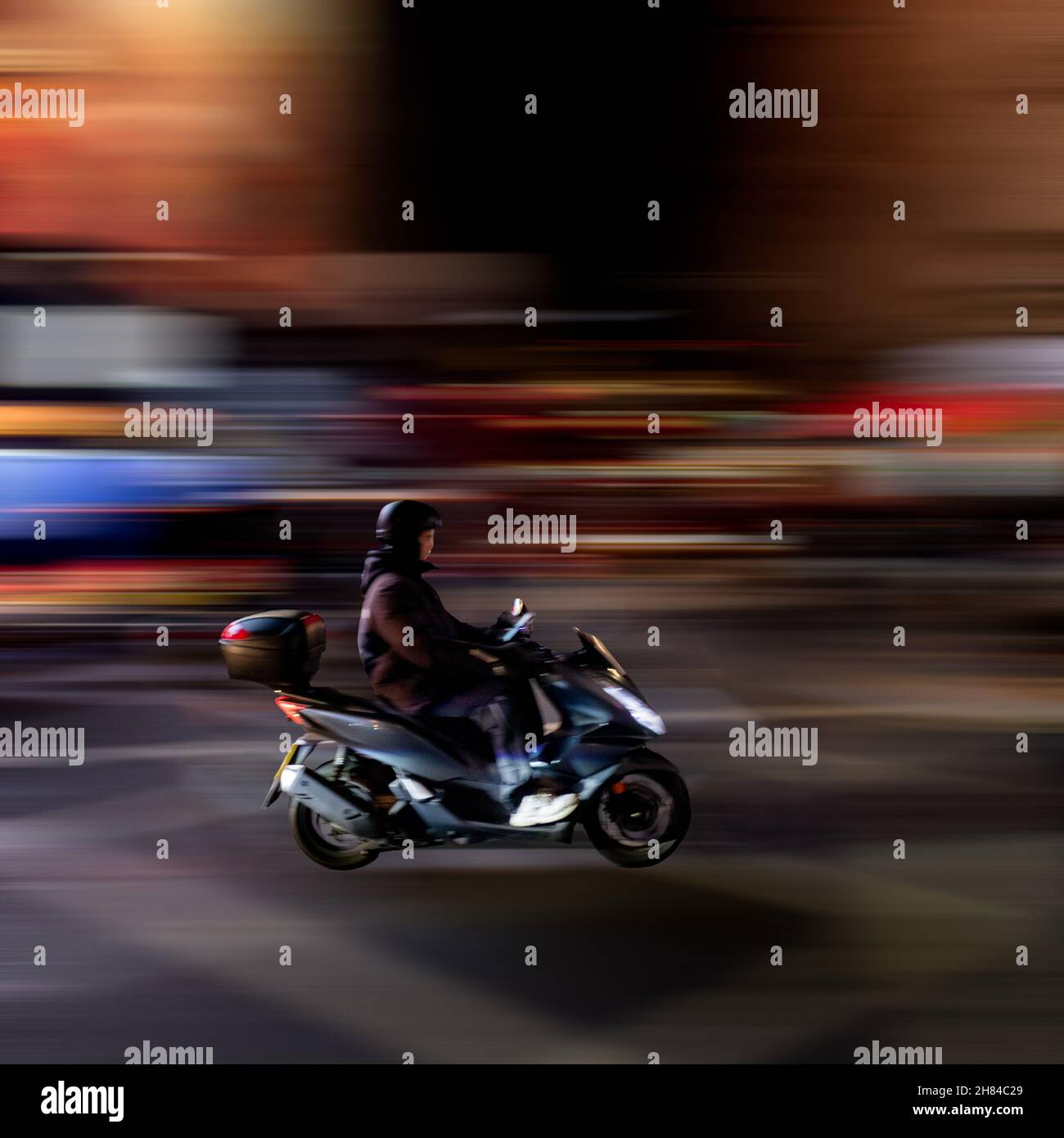 A panning shot of a person riding a moped with the lights of Piccadilly ...