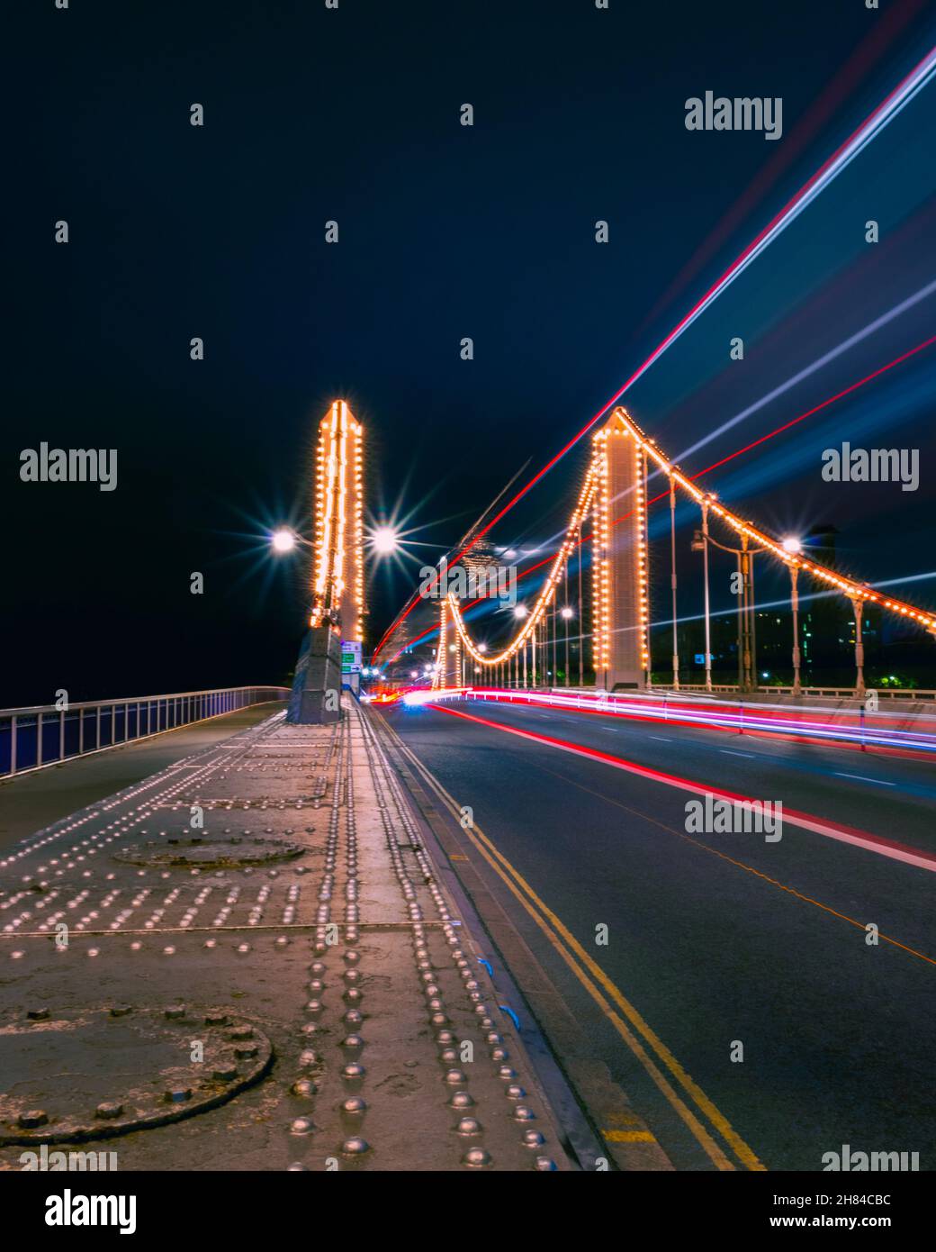 A bus speeding across Chelsea Bridge at night leaving dramatic light ...