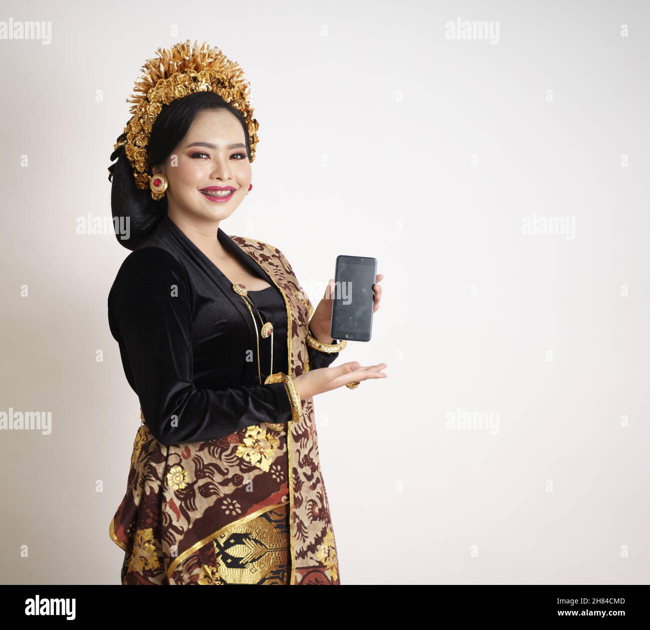 Smiling balinese woman wearing traditional clothes showing mobile phone ...