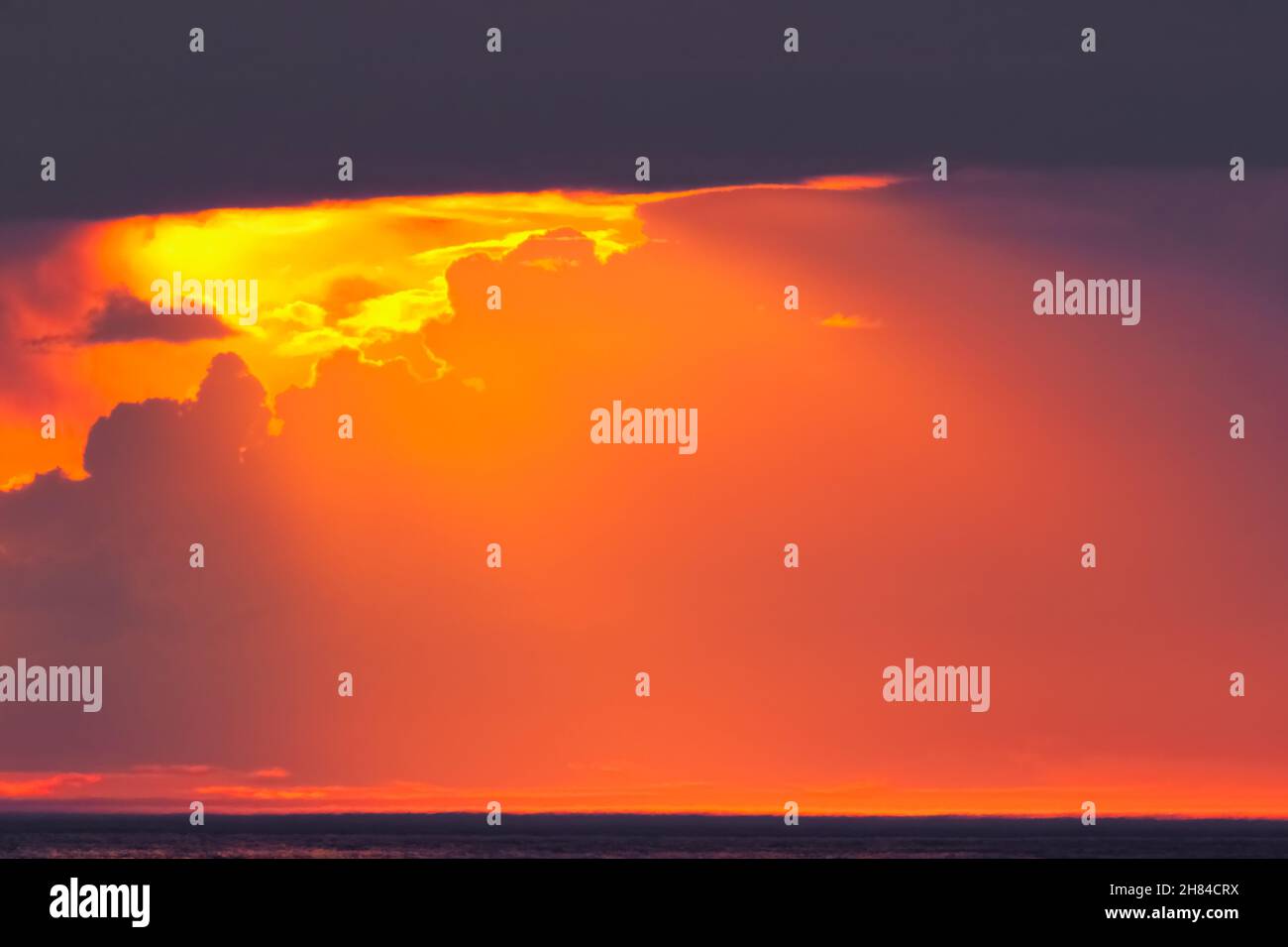 Pure bright orange sky between dark clouds overhead and blue water below Stock Photo - Alamy