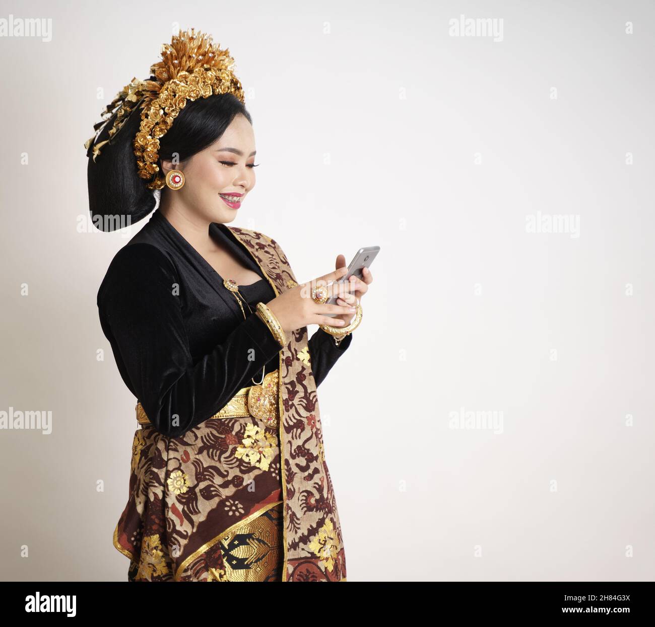 Smiling balinese woman wearing traditional clothes using mobile phone ...