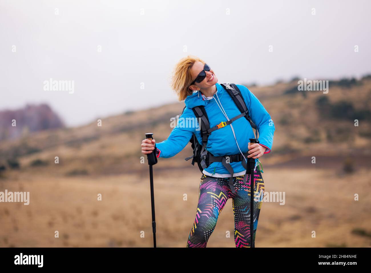 Hiking girl with poles and backpack standing on rocks. Windy autumn day ...