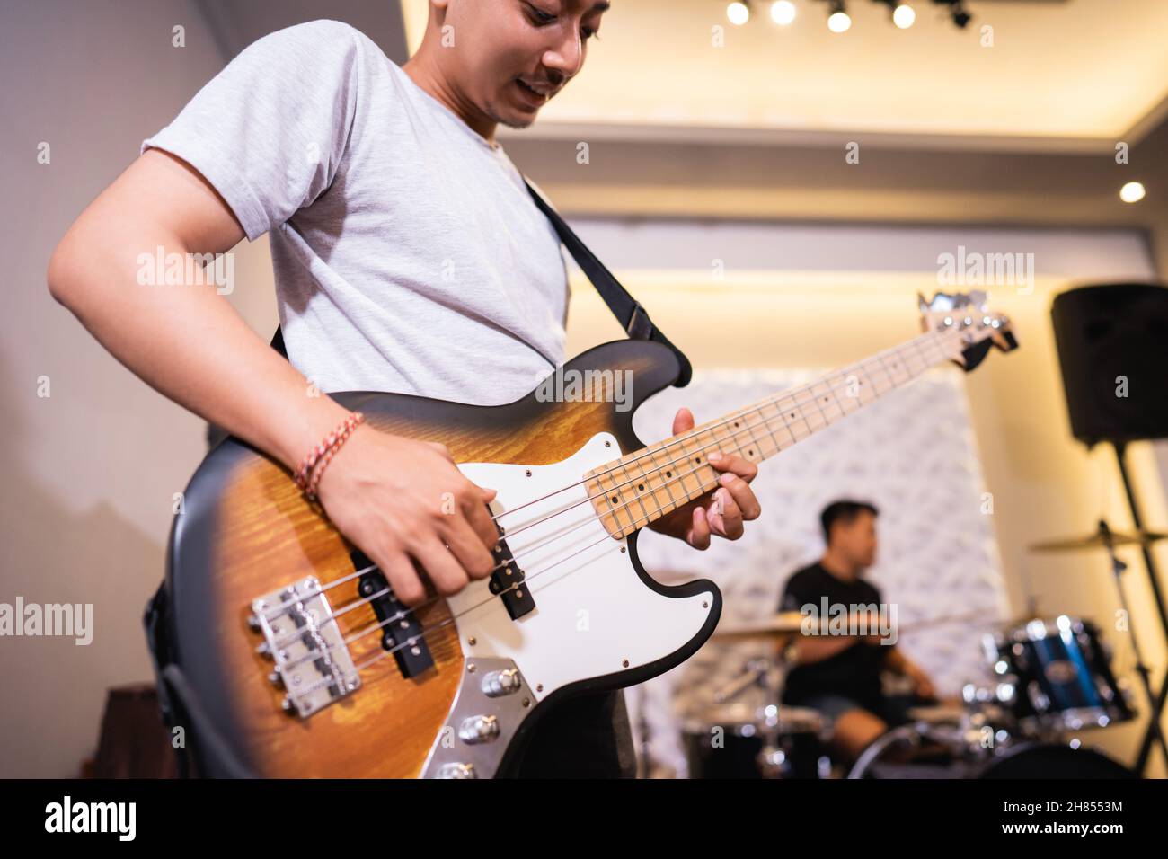 a male bassist plays an electric bass guitar during rehearsal with his ...