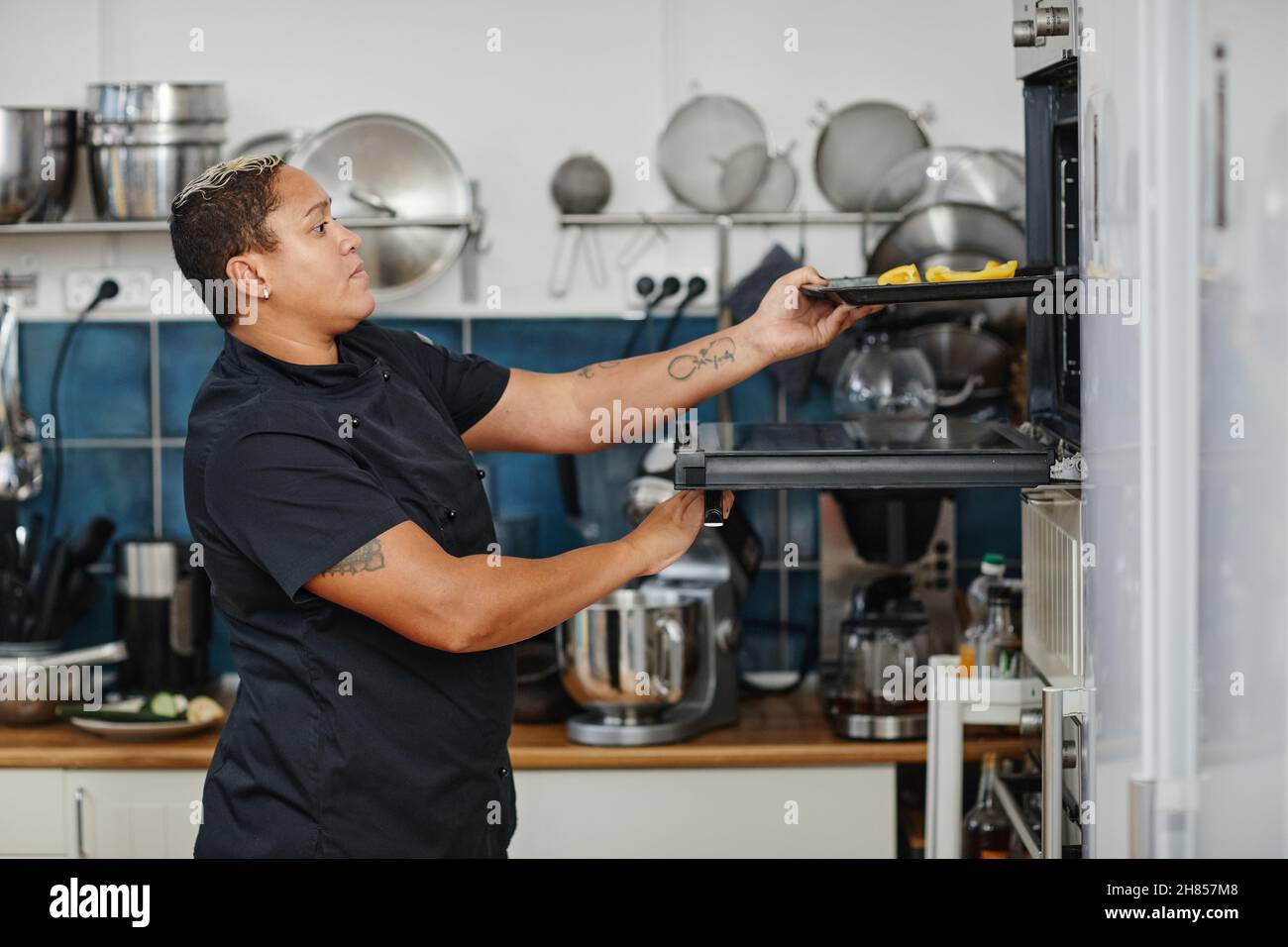 Side view portrait of tattooed female chef opening oven in professional ...