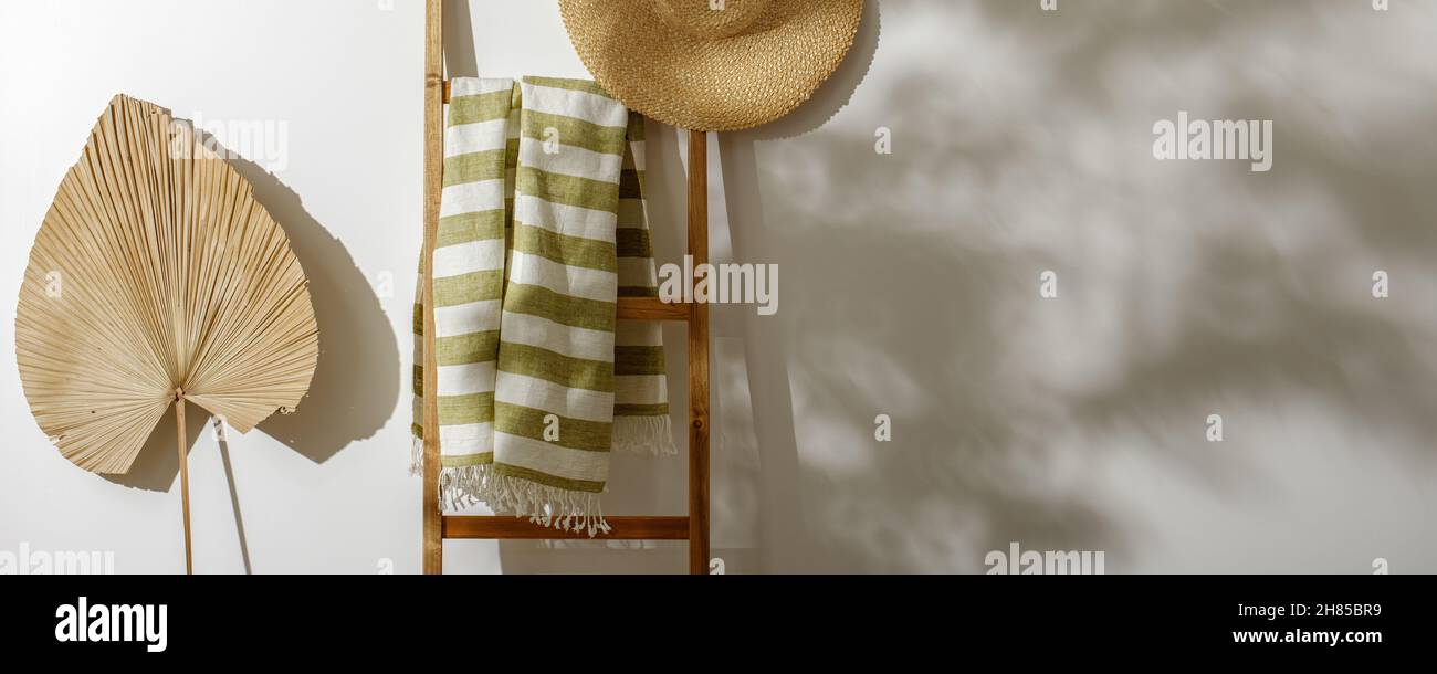 Organic linen beach towel on wood ladder, straw hat and dried palm leaf ...