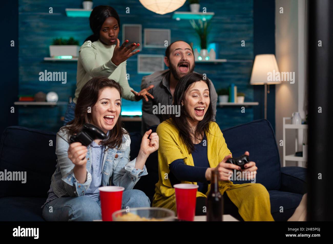 Smiling women friends sitting on couch winning videogames using gaming ...