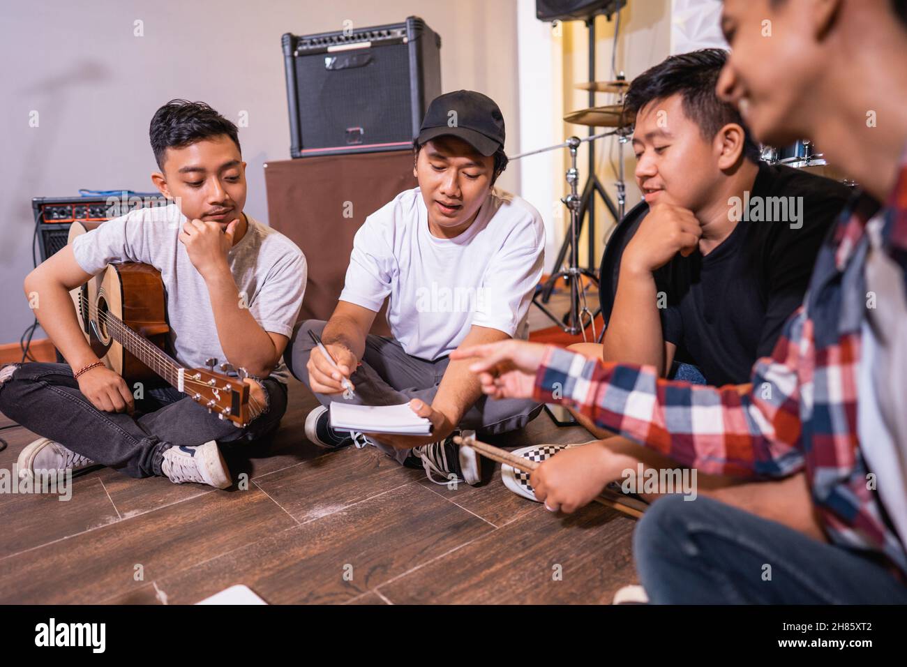 band members chat together sitting on the floor composing songs Stock ...