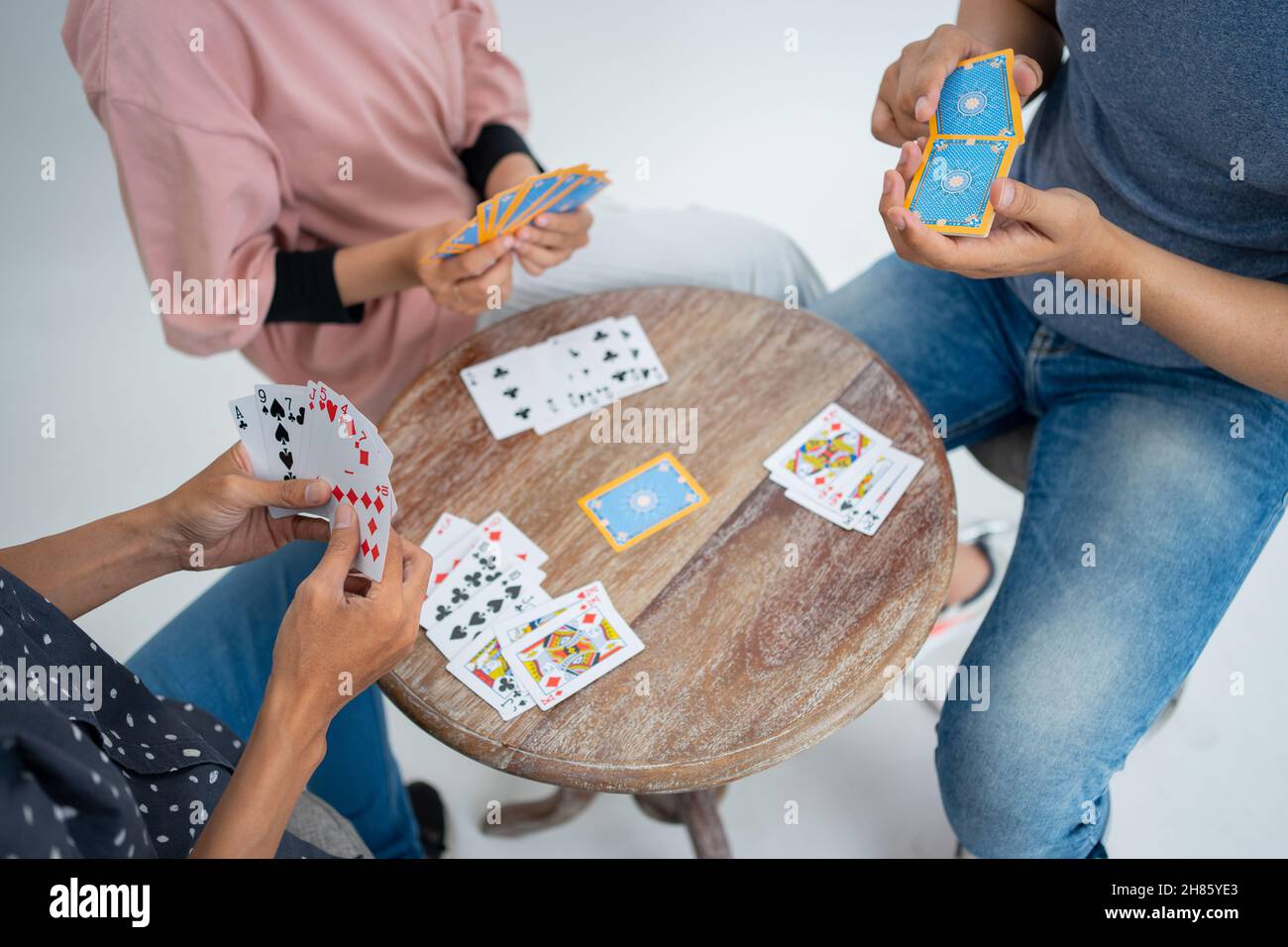 Three people holding cards while playing cards together Stock Photo - Alamy