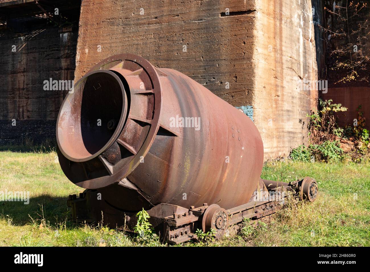 Rusting huge metal crucible on a wagon in a field of grass beside large ...