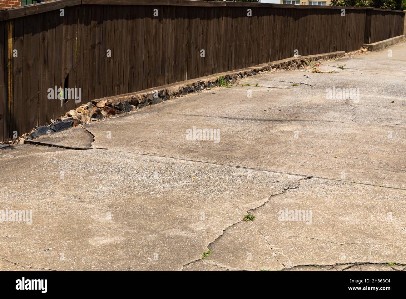 Cracked driveway with crumbling curb, dark wood fence running alongside ...
