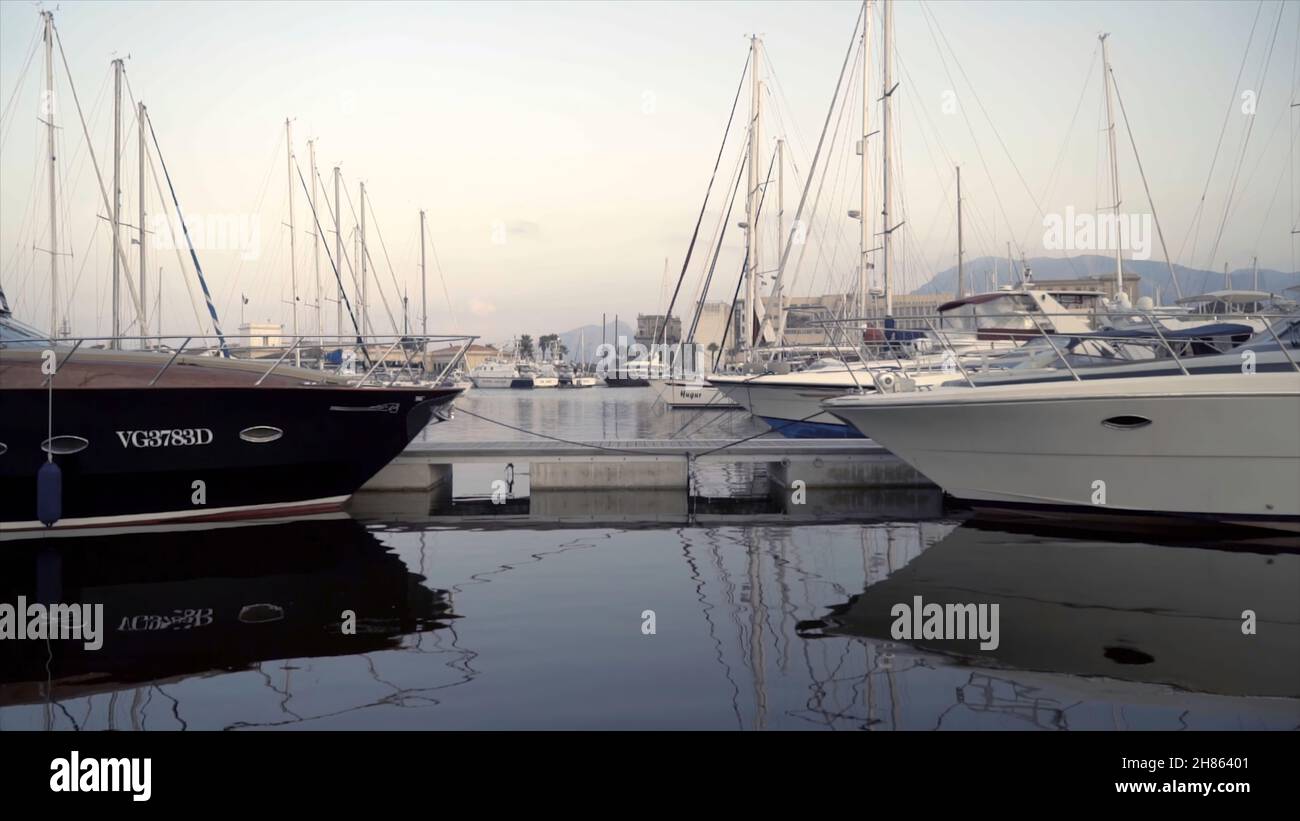 Beautiful yachts stand on pier on beautiful sky reflected in water. Action. Beautiful expensive ...