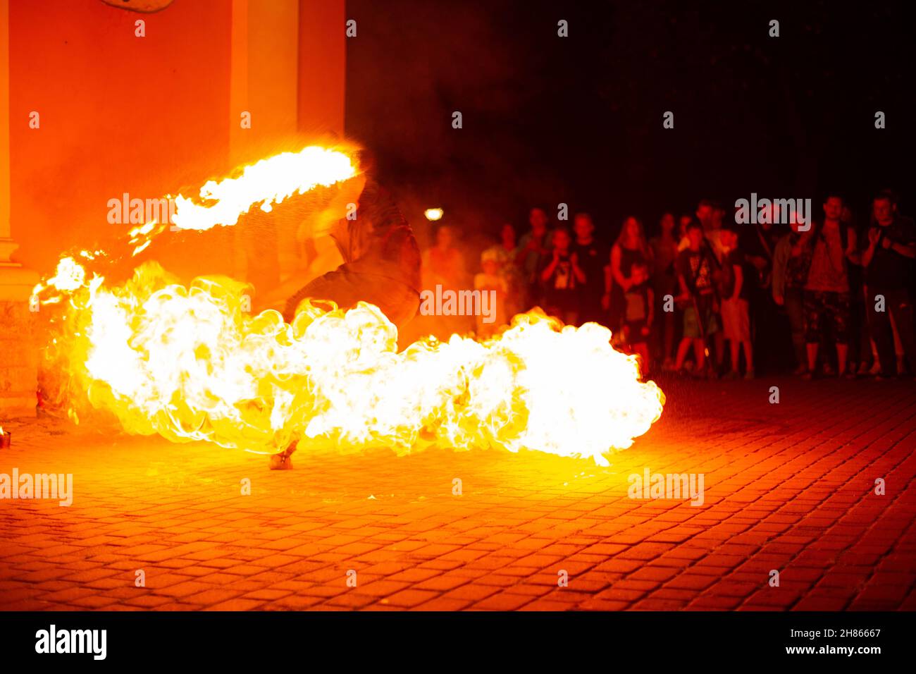 A guy makes a fire show on the street at night around a crowd of people ...
