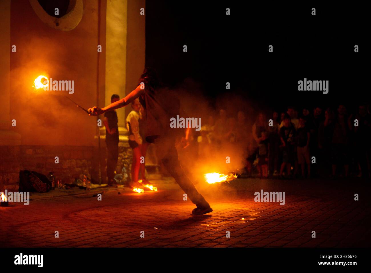 A guy makes a fire show on the street at night around a crowd of people ...