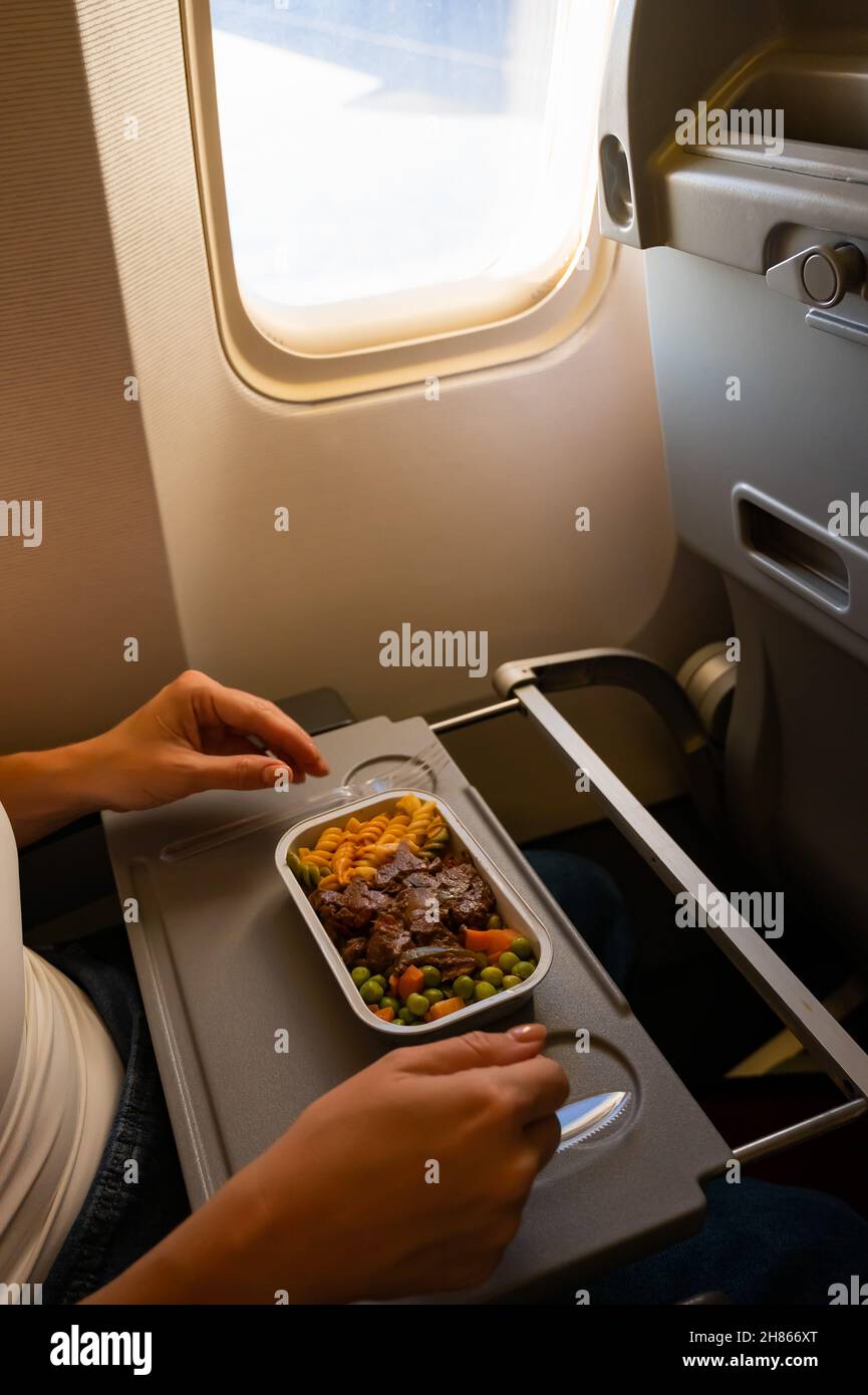 Caucasian woman flying in economy class and eating lunch from a tray ...