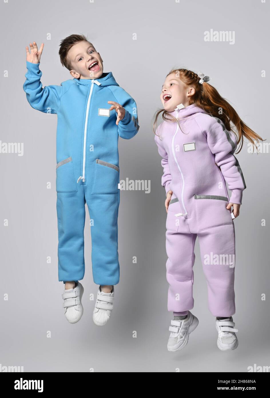Playful frolic kids boy and girl in blue and pink jumpsuits are jumping ...
