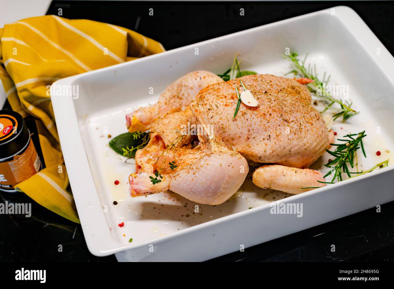 A whole dressed chicken with herbs spices in a white tray ready for ...