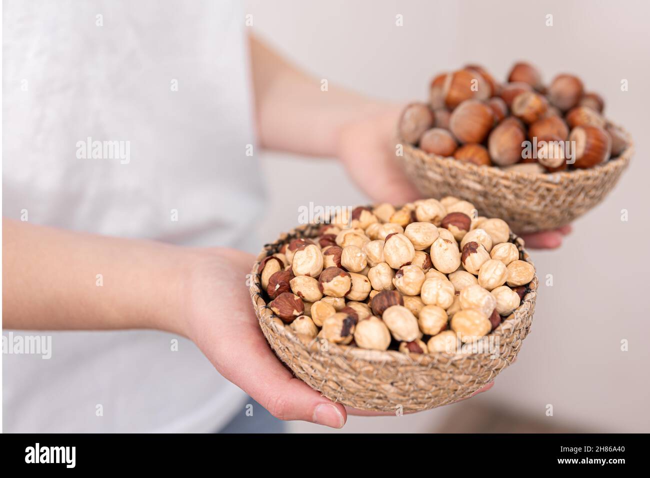 Close-up of a plate of hazelnuts and macadamia nuts in female hands ...