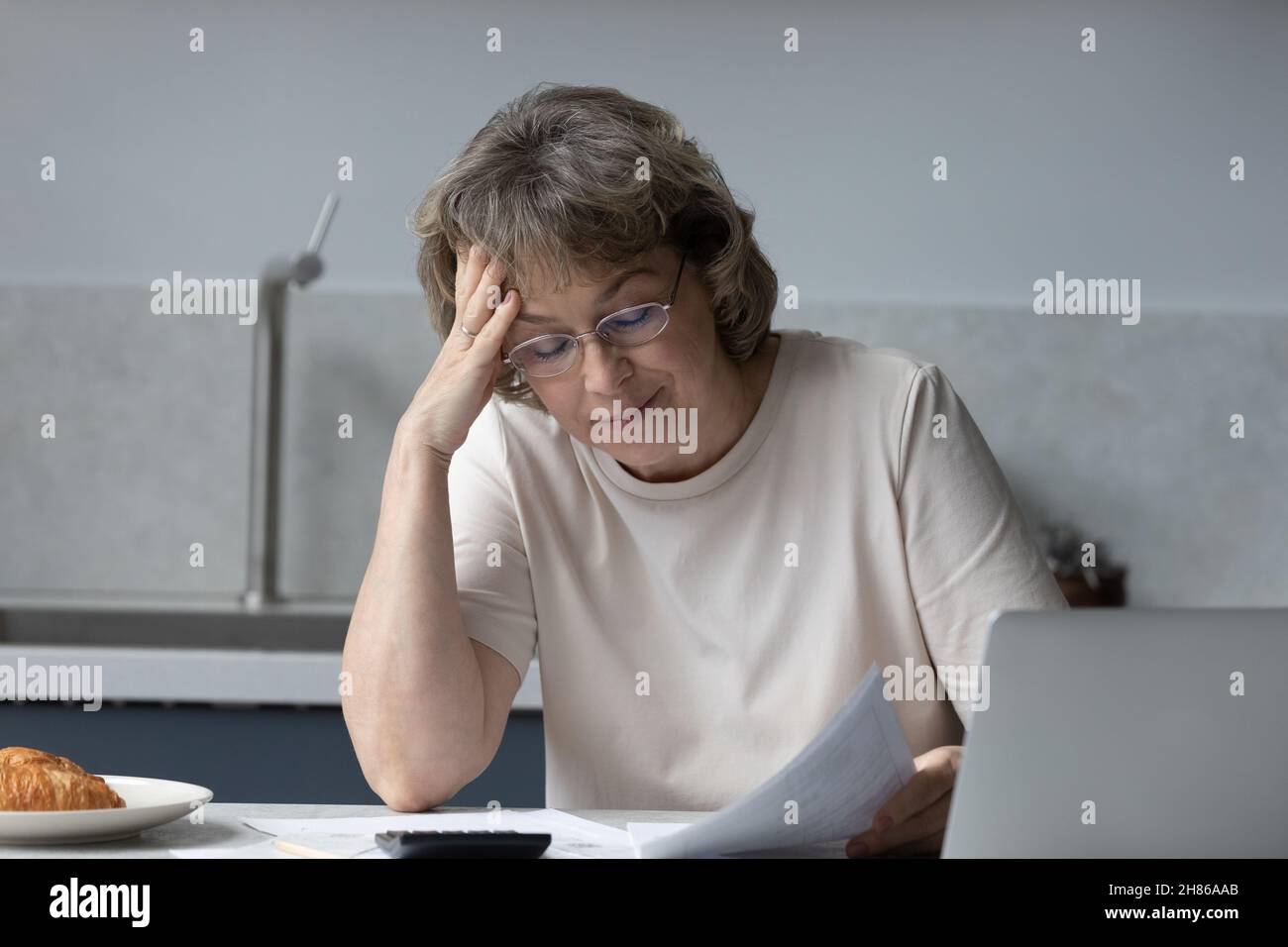 Concerned middle aged homeowner woman reading paper at laptop Stock ...