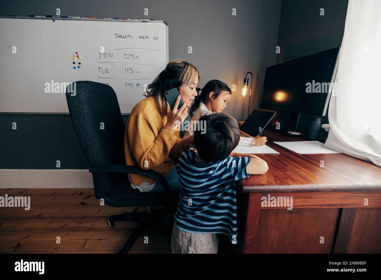 Working mother taking a phone call in her home office. Mother of two ...