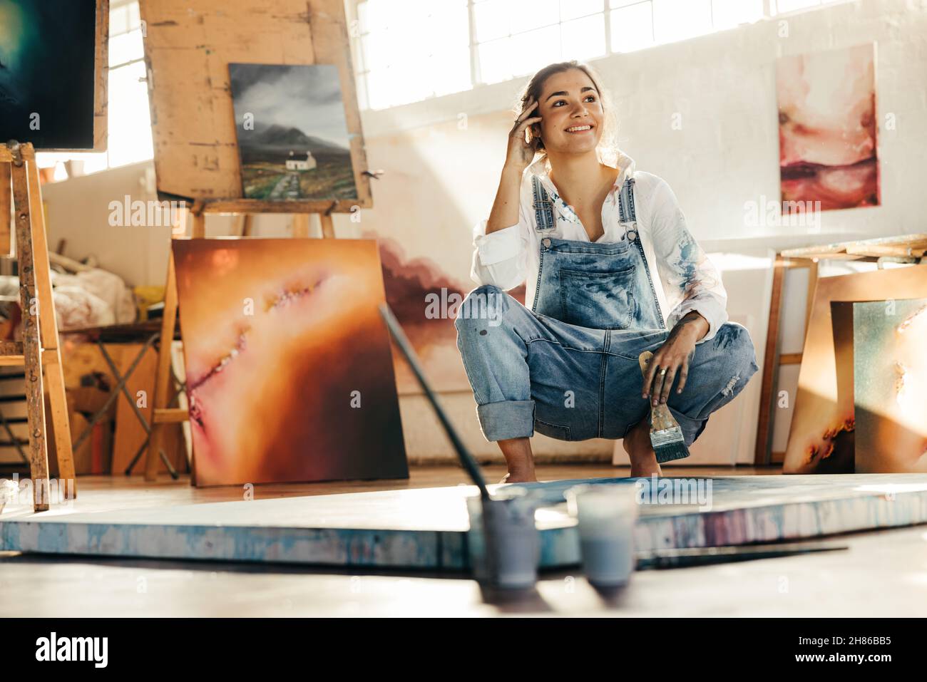 Thoughtful young artist smiling in her studio. Happy young painter ...