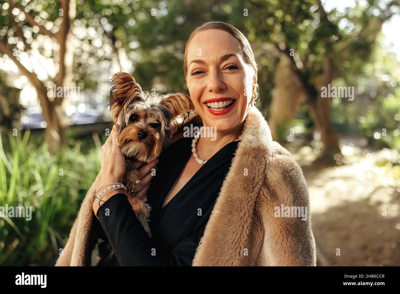 Happy posh woman smiling at the camera while holding her puppy outdoors ...