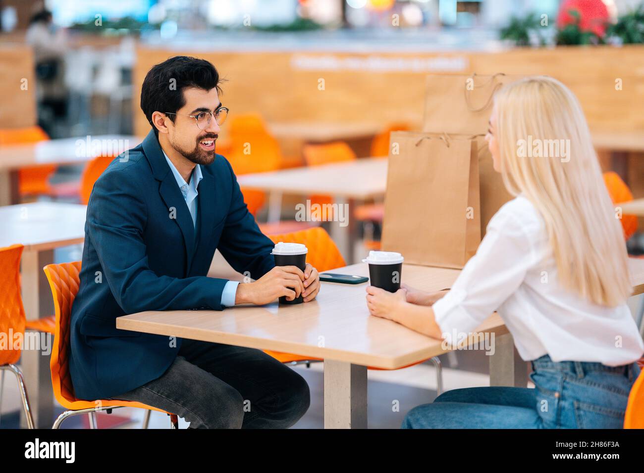 Side view of beautiful young couple drinking coffee and talking sitting ...