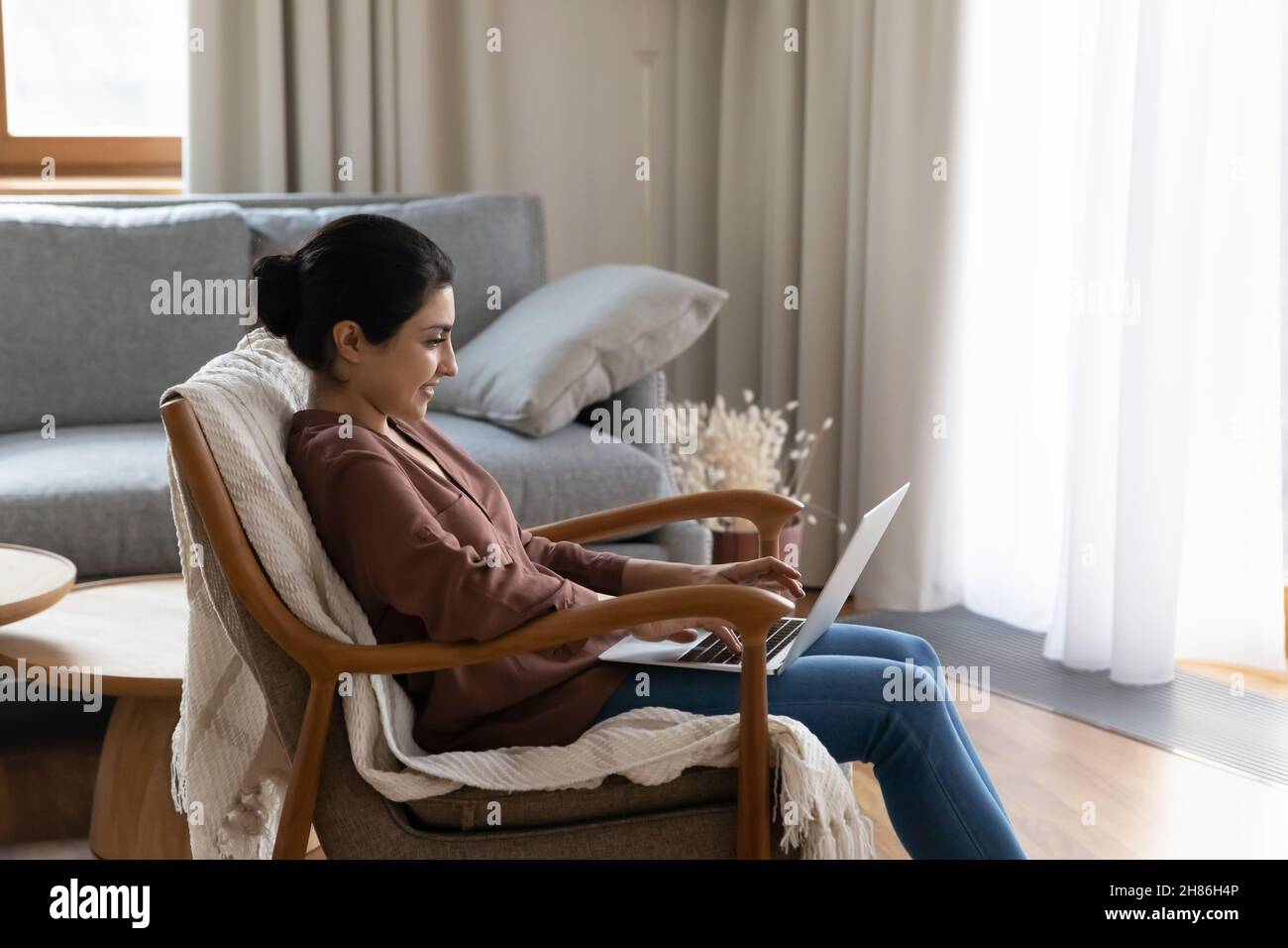 Smiling indian woman using computer, resting in armchair Stock Photo ...
