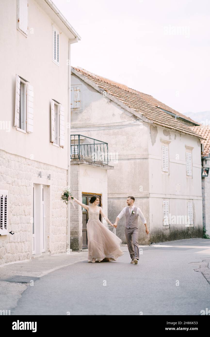 Bride and groom walk along the old town street past the stone buildings ...