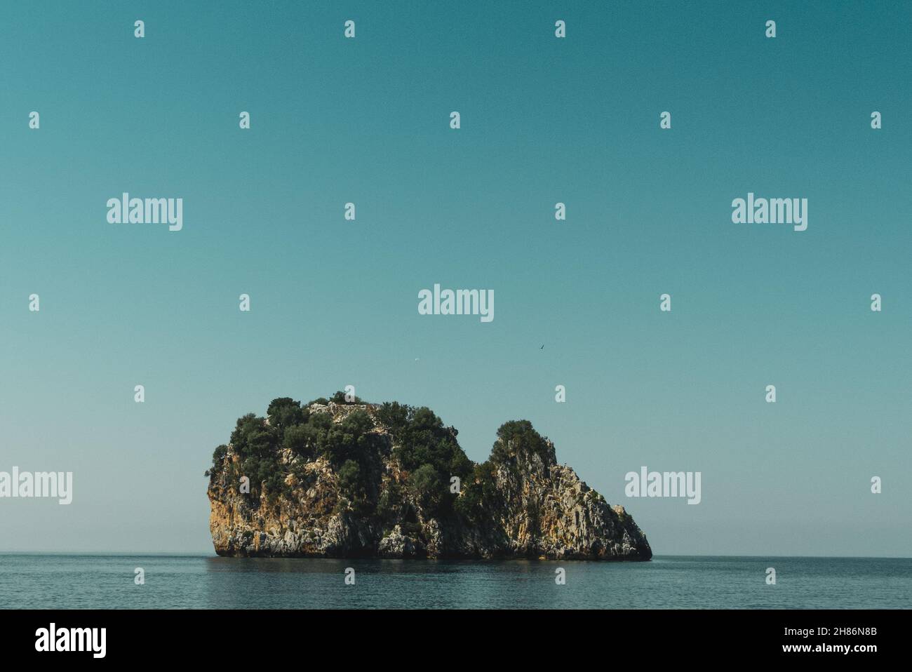 A beautiful scenery of a rocky cliff on blue water against a light sky ...