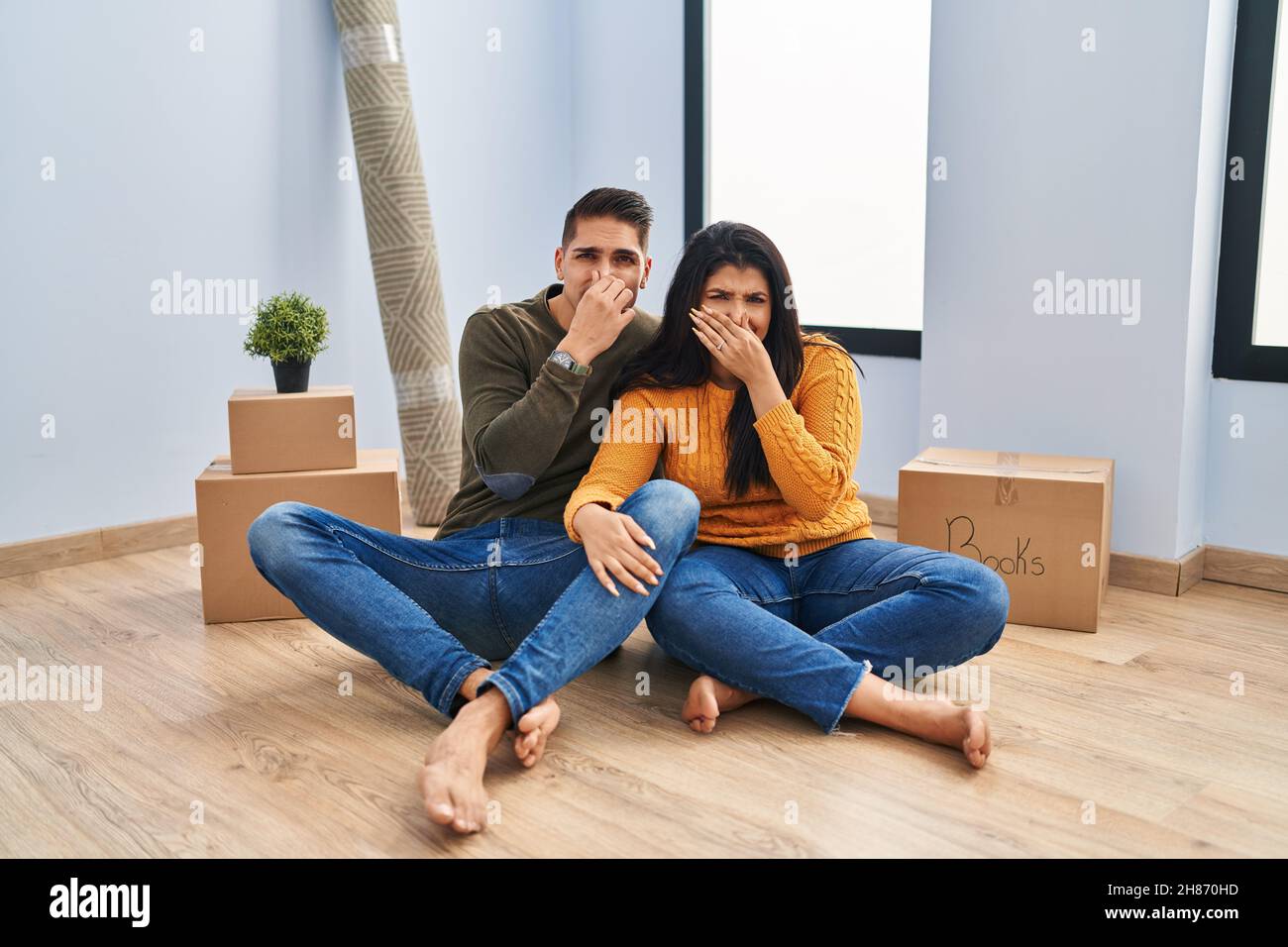 Young couple sitting on the floor at new home smelling something stinky ...