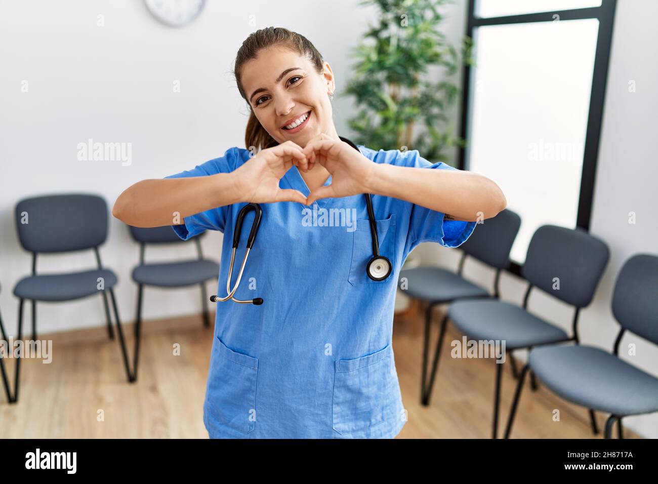 Young brunette doctor woman at waiting room smiling in love showing ...