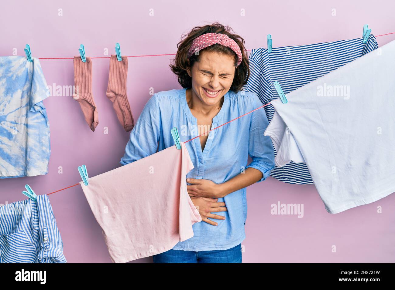 Young brunette woman doing laundry around string hangs with hand on ...