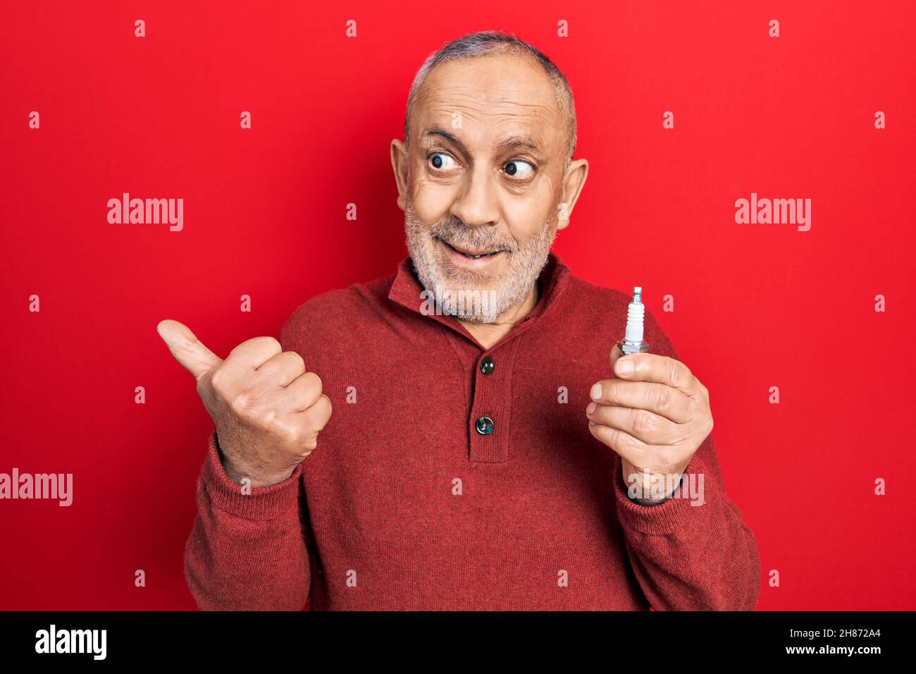Handsome mature man holding spark plug pointing thumb up to the side ...