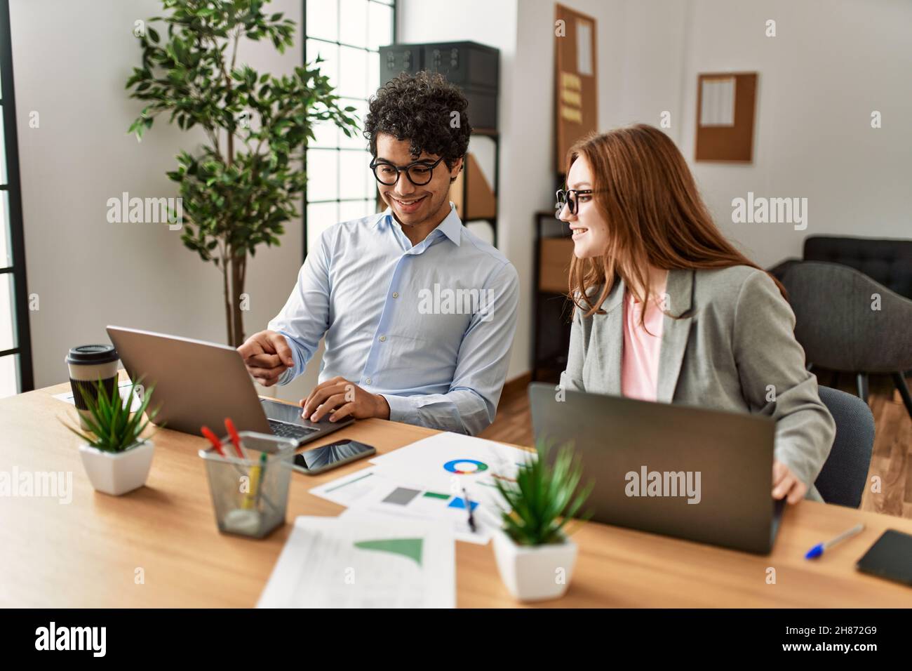 Two business workers smiling happy working using laptop at the office ...