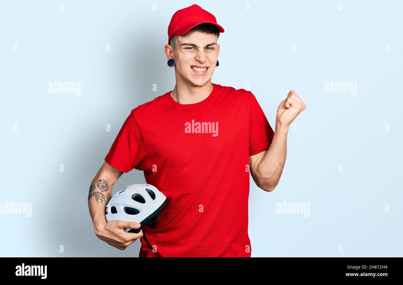 Young caucasian boy with ears dilation wearing delivery uniform and cap holding bike helmet ...