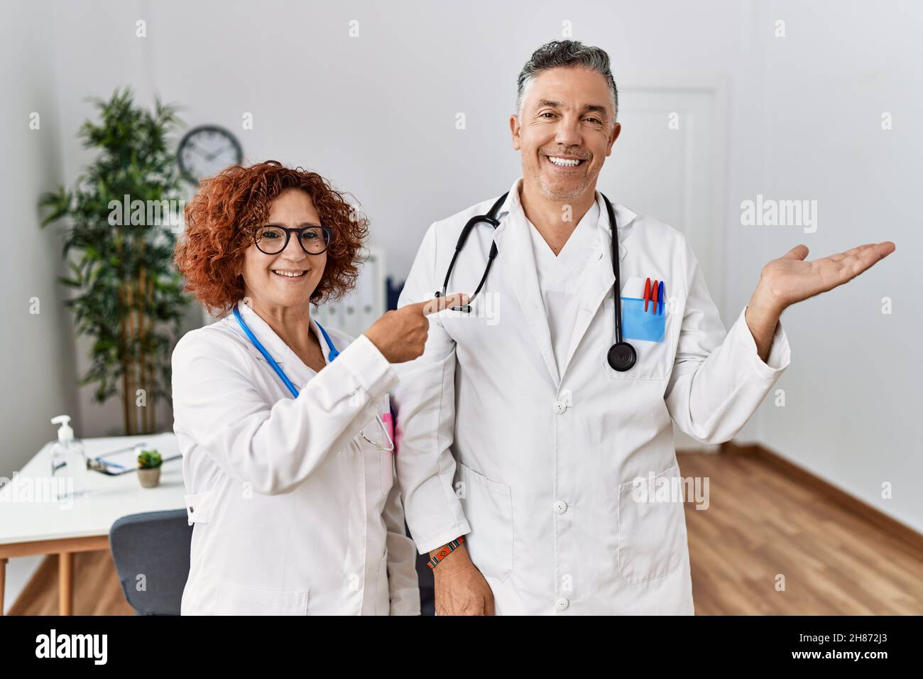 Two middle age doctors at medical clinic amazed and smiling to the ...