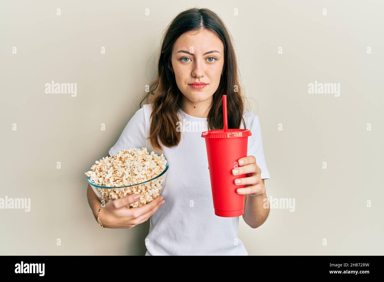 Young brunette woman eating popcorn and drinking soda relaxed with ...