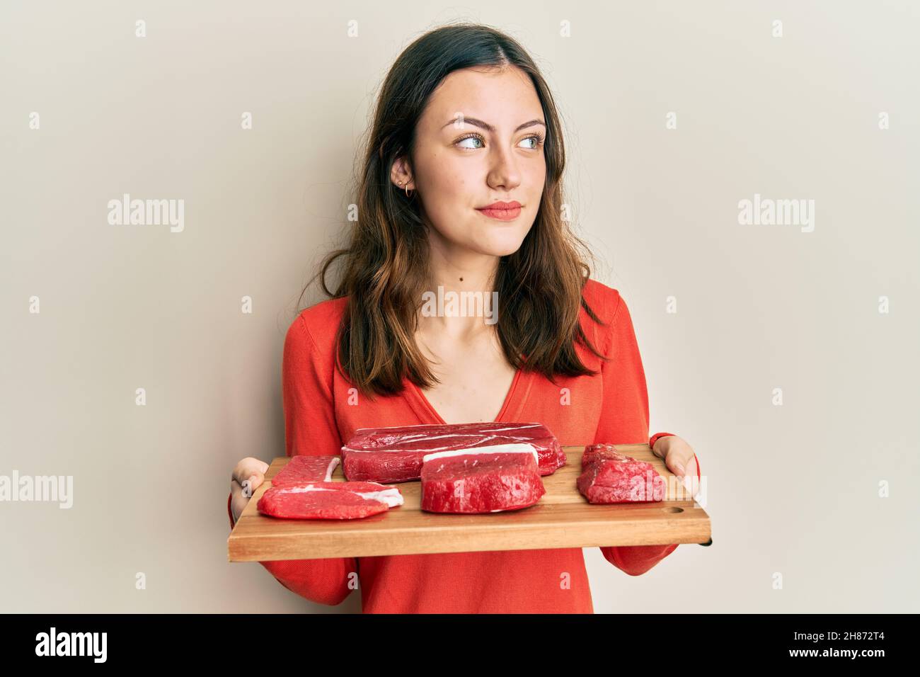 Young brunette woman holding board with raw meat smiling looking to the ...