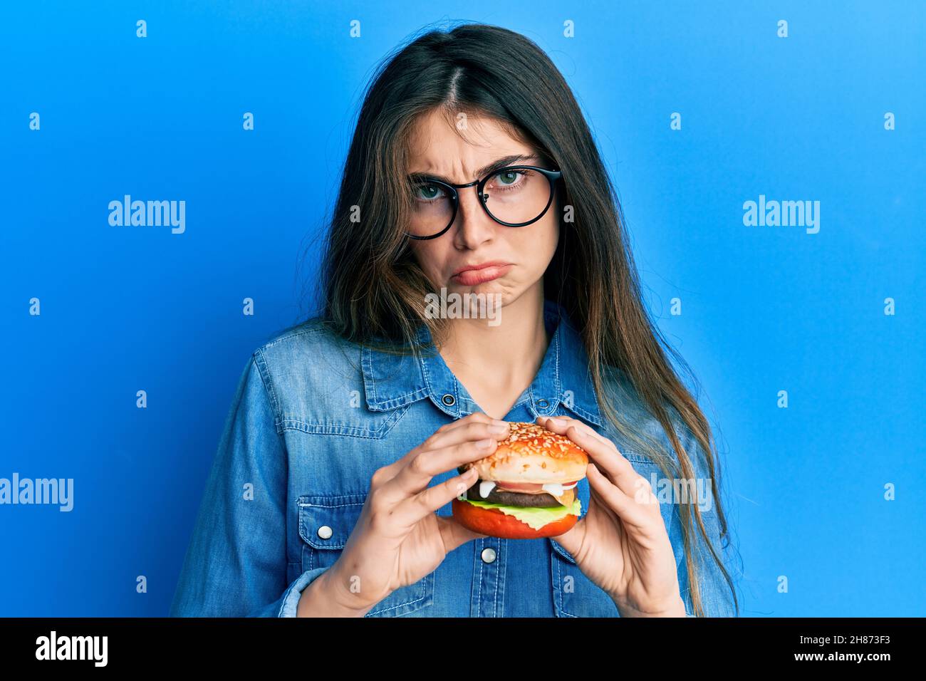 Young caucasian woman eating a tasty classic burger depressed and worry ...
