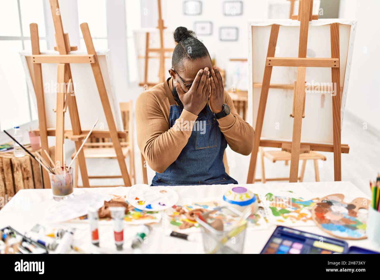 African american artist man at art studio with sad expression covering ...