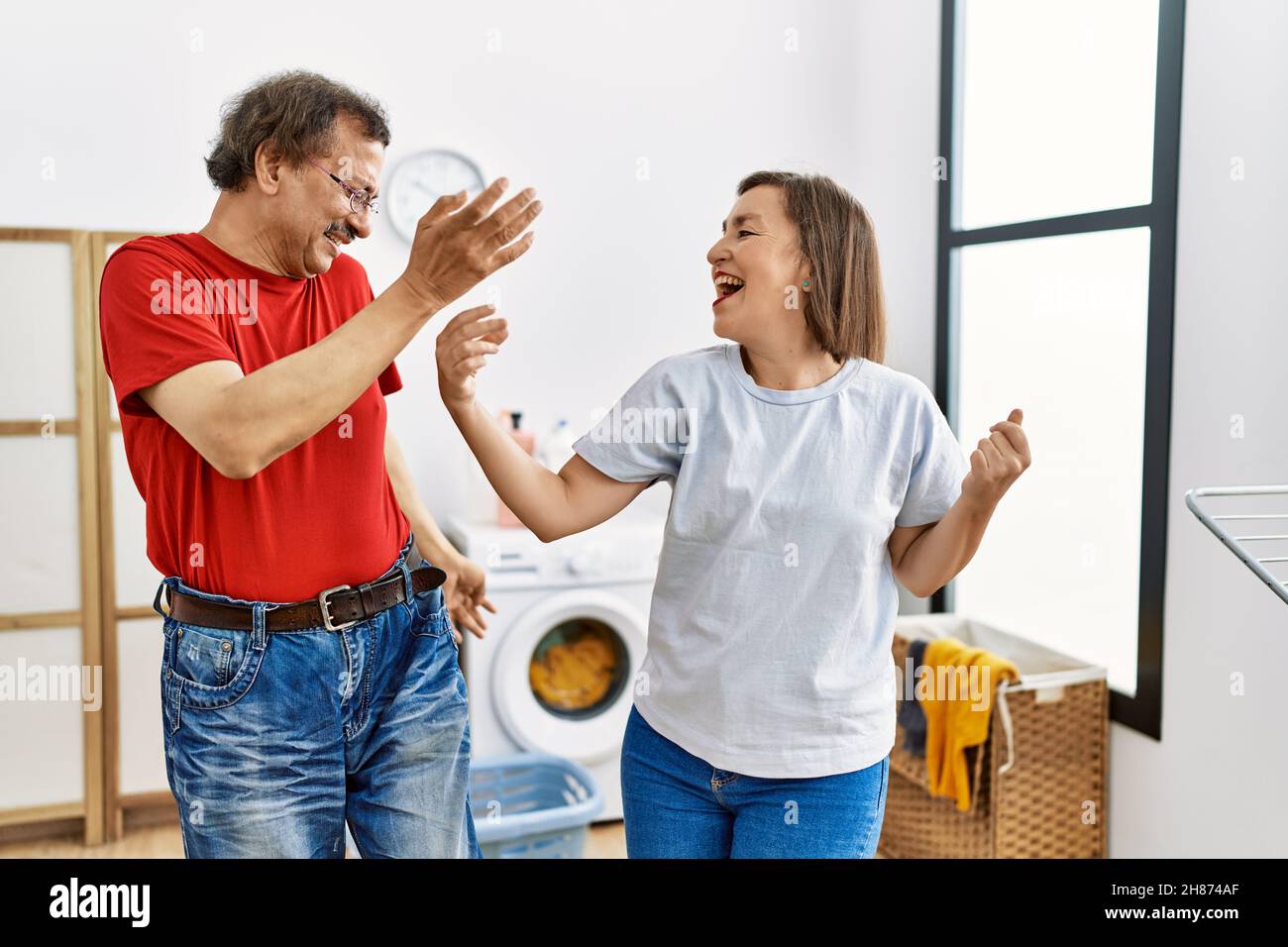 Middle age man and woman couple dancing waiting for washing machine at ...