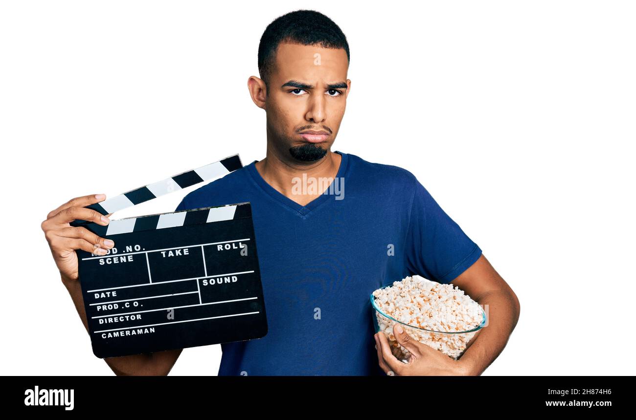 Young african american man eating popcorn holding film clapboard ...
