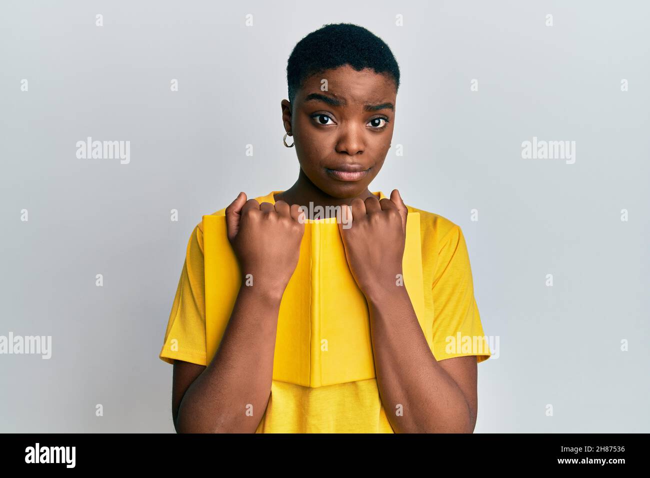 Young african american woman holding book skeptic and nervous, frowning ...