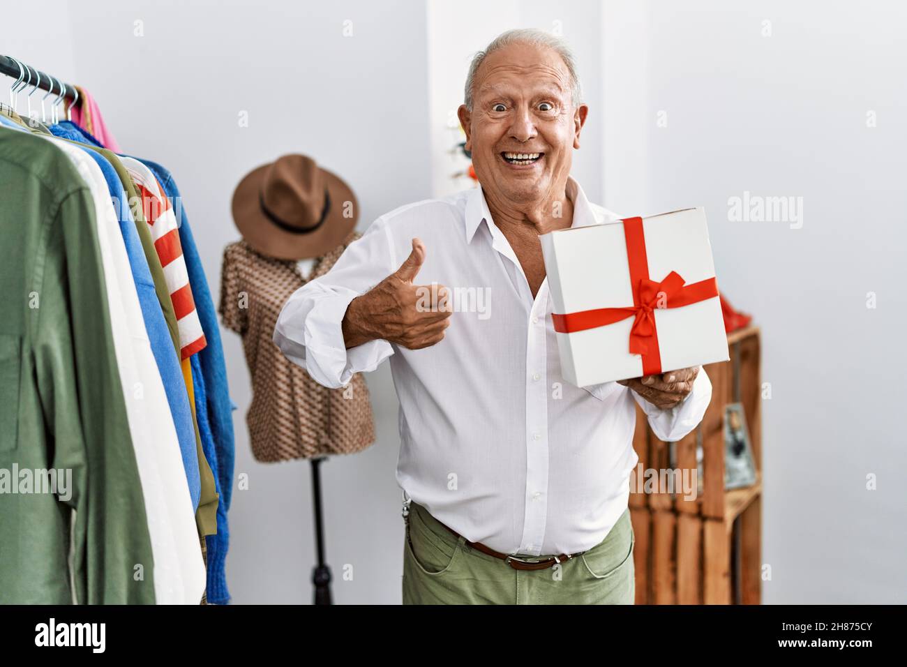 Senior man holding gift at retail shop smiling happy and positive ...